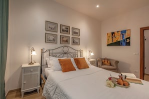 Quarto bem arrumado com cama, mesas de cabeceira, uma cadeira e um quadro na parede.