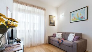 Uma sala de estar com um sofá cinza, uma mesa de centro de vidro, um vaso com flores amarelas e um quadro na parede.
