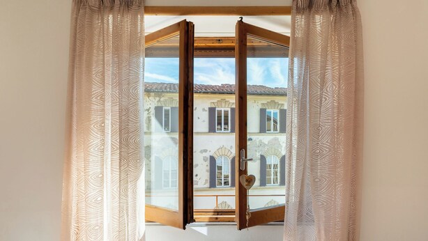 Quarto com janela emoldurada em madeira e vista para um edifício com várias janelas e persianas.