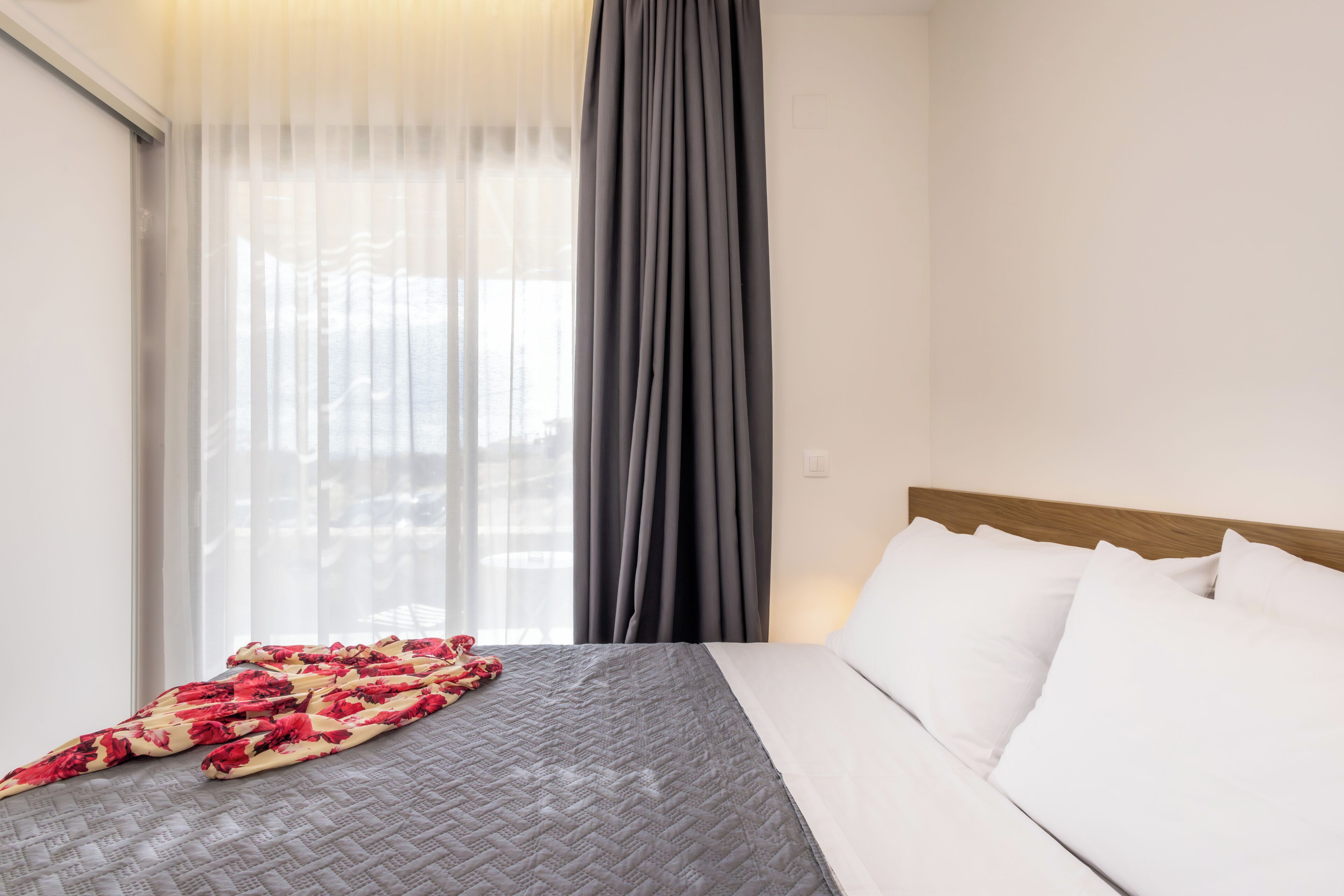 Quarto de hotel com cama, janela com cortinas finas e vista para edifícios.