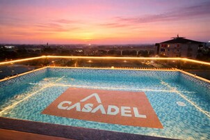 Uma piscina com o logotipo CASADEI, rodeada por um deck revestido e vista para o pôr do sol.