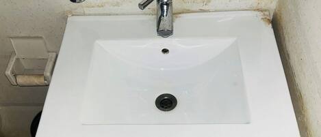 Uma pia de banheiro com uma torneira, um dosador de sabonete e um suporte para papel higiênico.