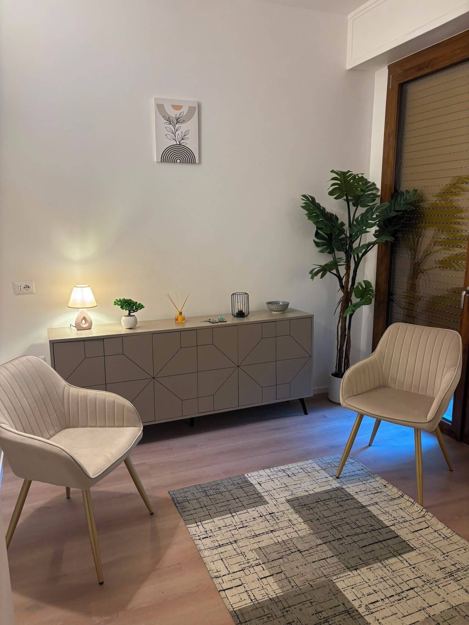 Uma sala de estar moderna com duas cadeiras, um aparador, um abajur e um vaso com planta.