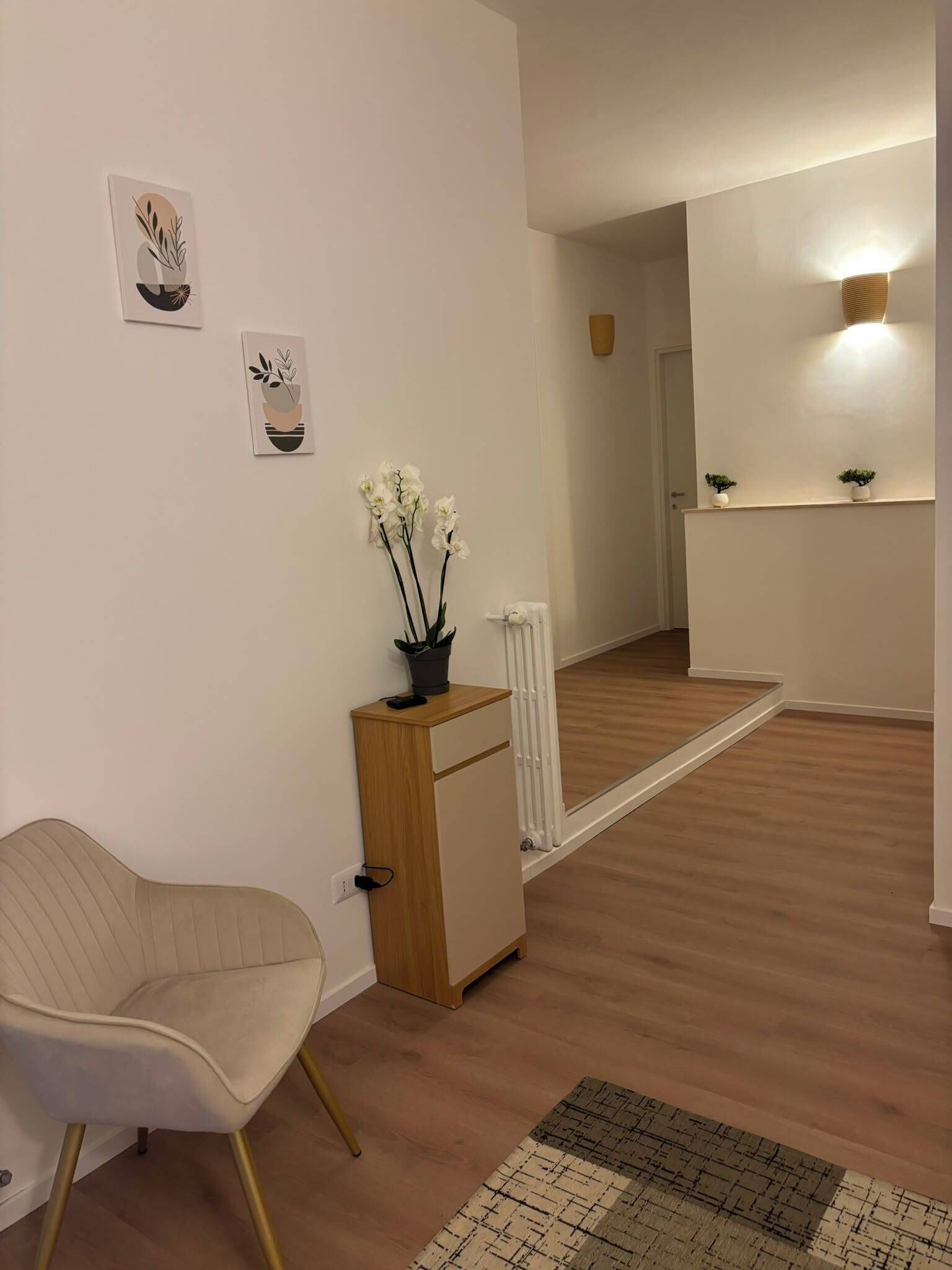 Um quarto com uma cadeira, um radiador, uma mesinha com uma planta e obras de arte na parede.