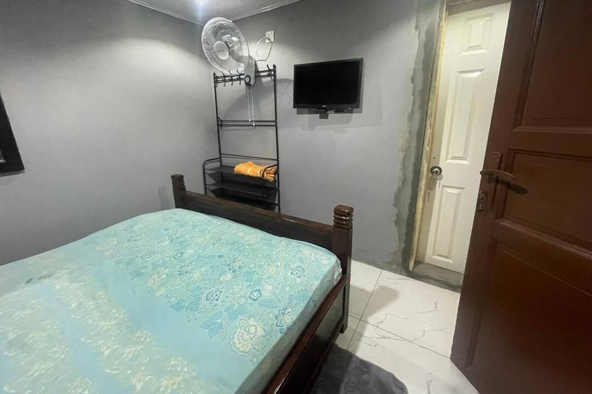 Quarto com cama, ventilador, televisão e porta.