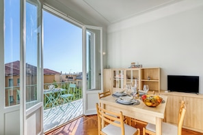 Uma área de refeições com uma mesa posta para dois, uma televisão e vista da cidade através de grandes janelas.