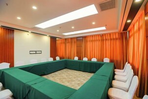 Uma sala de conferência com uma mesa comprida, cadeiras brancas e cortinas laranja.