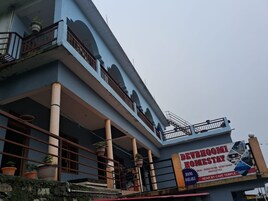 Um edifício de dois andares com uma placa anunciando 'DEVROOMI HOMESTAY' e quartos disponíveis.