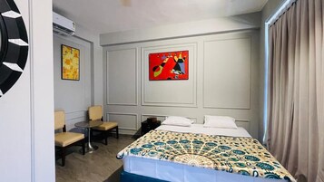 Quarto de hotel com uma cama, uma escrivaninha, duas cadeiras e obras de arte nas paredes.
