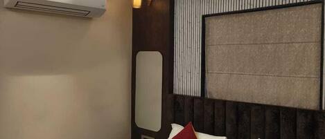 Quarto de hotel com uma cama, ventoinha no teto, ar condicionado e espelho fixado na parede.