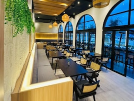 Uma sala de jantar moderna com mesas compridas e cadeiras, janelas amplas e teto de madeira.