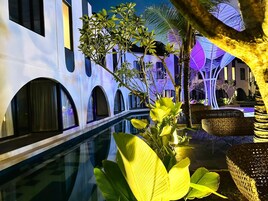 Piscina com um edifício moderno ao fundo, rodeada por vegetação e área de estar externa.