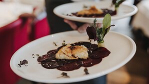 Um prato com um pedaço de peixe, um molho escuro e alguns vegetais.