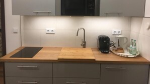 Uma cozinha moderna com armários cinza, micro-ondas de aço inoxidável, bancada de madeira, pia e cafeteira.