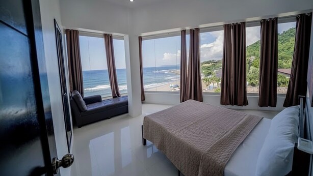 Quarto com cama grande, área de estar junto à janela e vista para o oceano.
