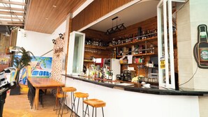 Uma área de bar com banquetas de madeira, um balcão com diversos frascos e um mural na parede.