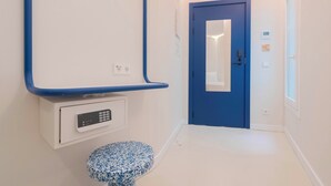 Um corredor com uma porta azul, um banco branco e um painel de controle na parede.