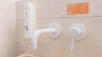 Casa de banho com dispensador de sabonete líquido, torneira e sinal de reciclagem.