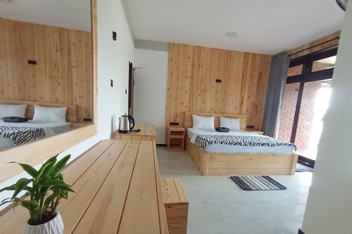 Quarto moderno com paredes de painel de madeira, duas camas com roupa de cama estampada em padrão de zebra, um banco de madeira, uma planta em vaso e uma pequena mesa.