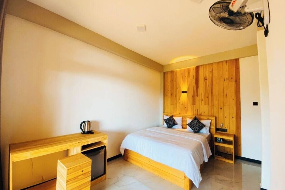 Quarto com cama de madeira, mesas de cabeceira, escrivaninha e ventoinha de teto.