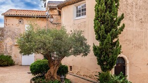 Um pátio com caminho de pedras, uma árvore e um edifício com telhado de azulejos e uma porta.
