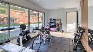 Uma academia com equipamentos de ginástica, grandes janelas e vista para uma piscina.