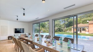 Uma sala de reuniões ampla com uma mesa comprida, cadeiras e uma televisão. Grandes janelas oferecem vista para uma piscina e áreas verdes.