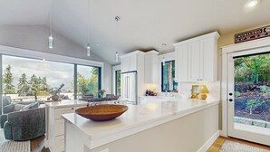 Uma cozinha moderna com armários brancos, uma ilha grande e vista para o exterior.