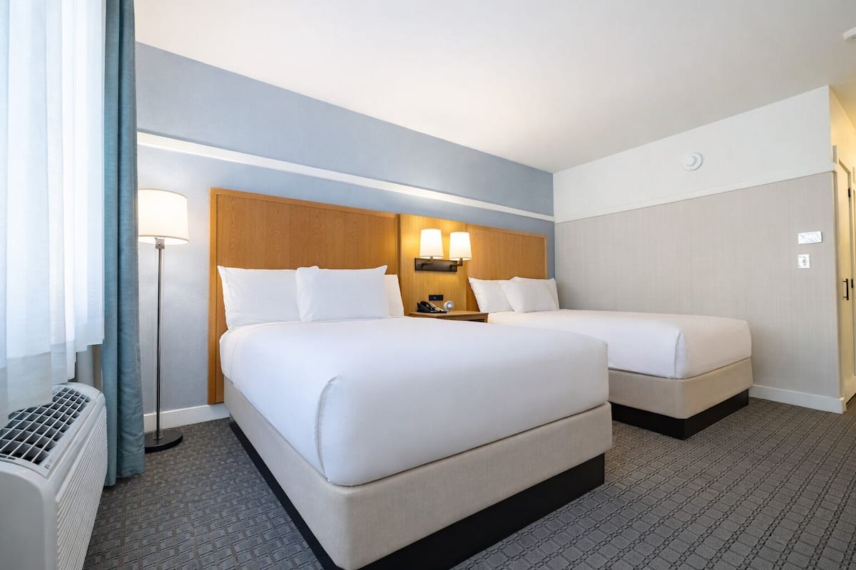 Quarto de hotel com duas camas, uma escrivaninha, um abajur e um aquecedor.