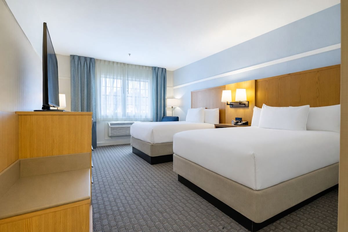 Quarto de hotel com duas camas, televisão, escrivaninha e janela com cortinas.