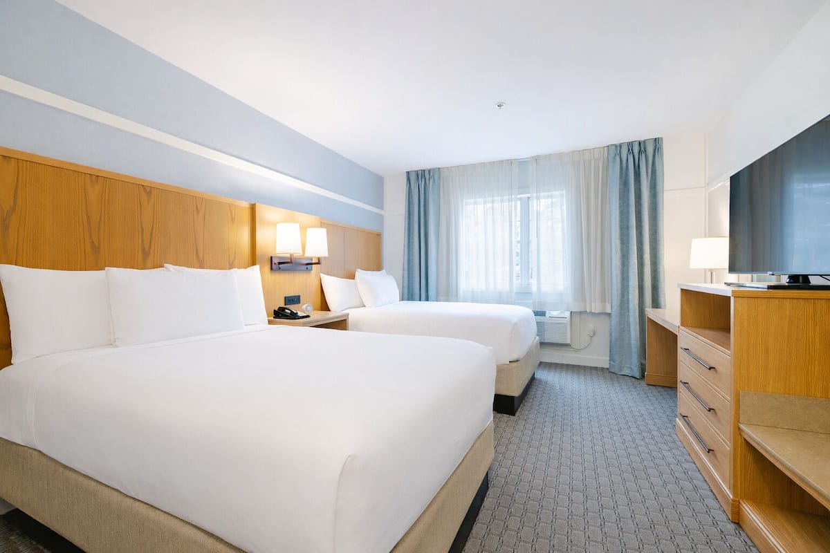 Quarto de hotel com duas camas, uma escrivaninha, televisão e janela com cortinas.