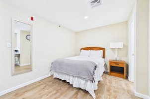 Quarto com cama, mesa de cabeceira, luminária e espelho na parede.