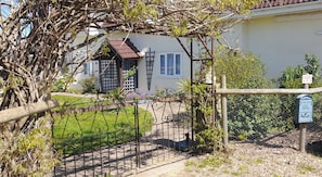 Uma entrada fechada por portão com uma caixa de correio, um pequeno jardim e uma casa com telhado vermelho e paredes brancas.