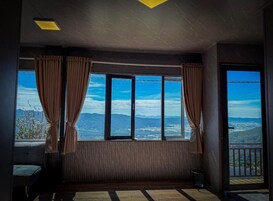 Quarto com uma grande janela com vista para as montanhas, um espaço de estar pequeno e uma varanda.