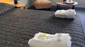 Quarto de hotel com uma cama grande, uma cadeira, uma mesinha com um tabuleiro e um quadro de uma praia.