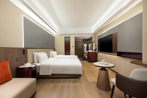 Quarto de hotel com uma cama grande, televisão, escrivaninha e uma cadeira.