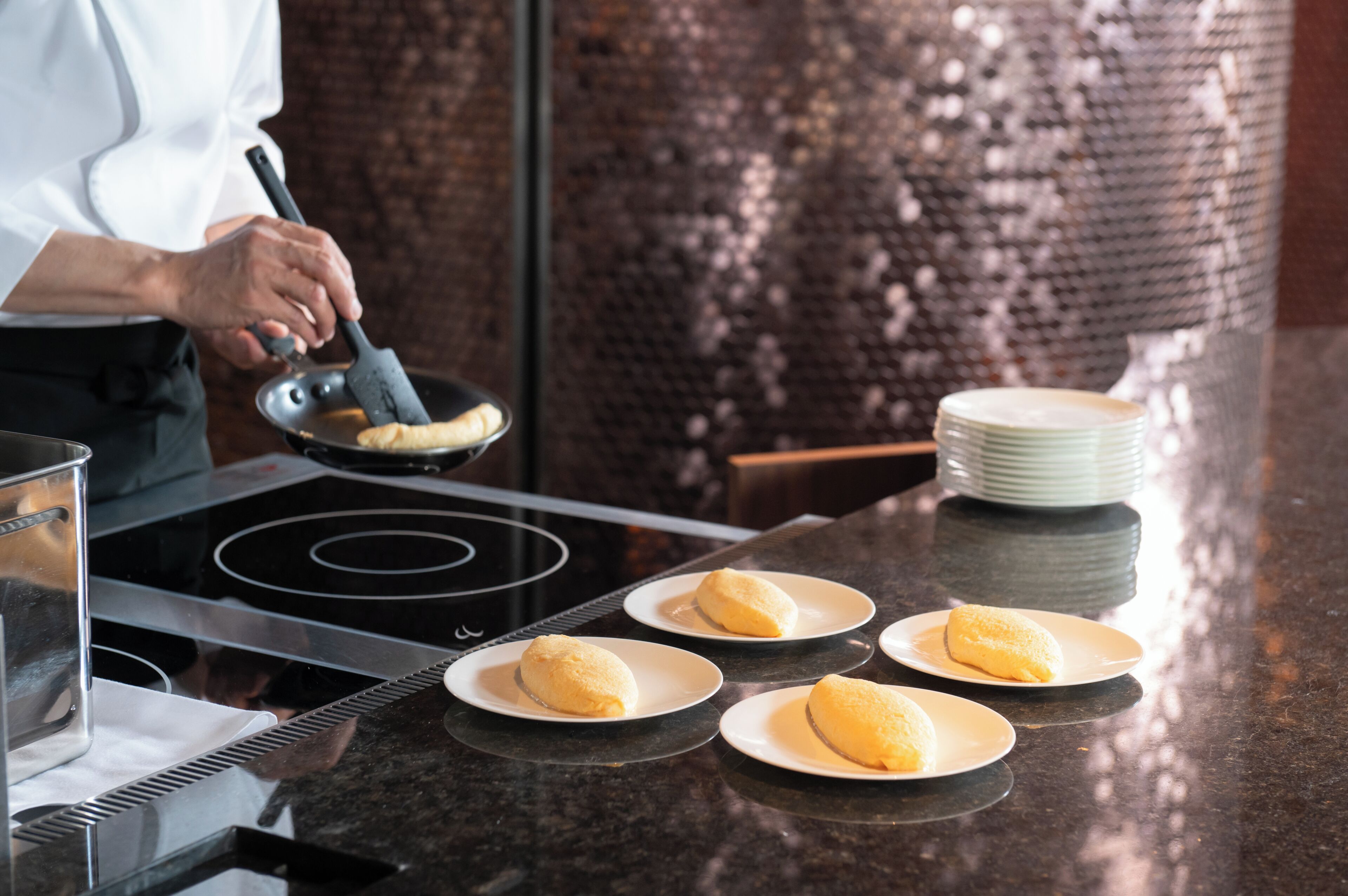 Uma cozinha com alguém cozinhando, uma pilha de pratos e um fogão de aço inoxidável.