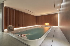 Um spa moderno com uma banheira grande, paredes revestidas de madeira e uma pequena área de estar com uma toalha.