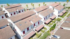 Uma área residencial costeira com edifícios de telhado em terracota, praia e palmeiras.