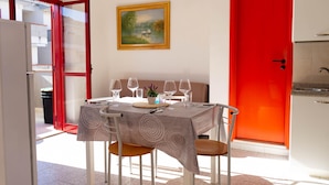 Uma sala de jantar com uma mesa posta para seis pessoas, uma porta vermelha e um quadro na parede.