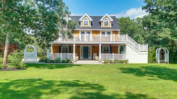 Uma casa de dois andares com varanda da frente, escada e gramado bem cuidado.