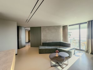 Sala de estar moderna com um sofá seccional cinza, uma pequena mesa redonda e uma grande janela com vista para o exterior.