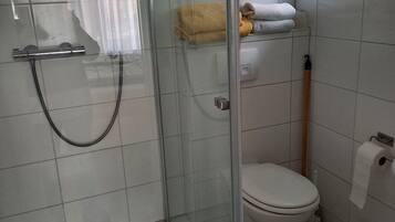 Casa de banho com chuveiro envidraçado, sanita e lavatório.