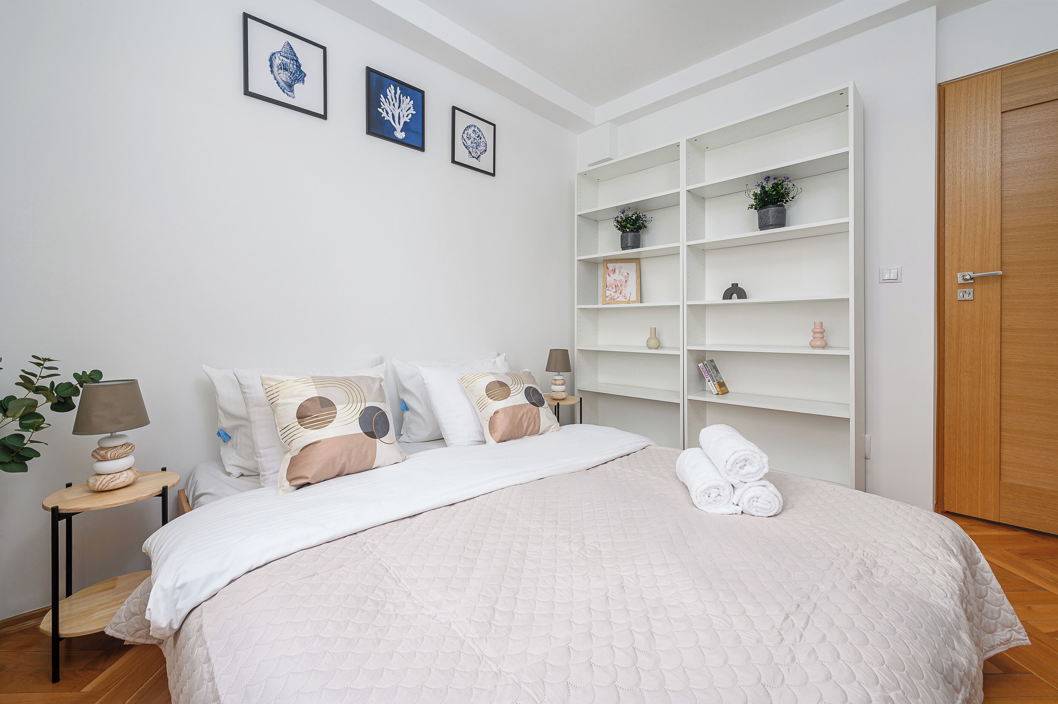 Quarto bem arrumado com cama, mesas de cabeceira, estante e porta.
