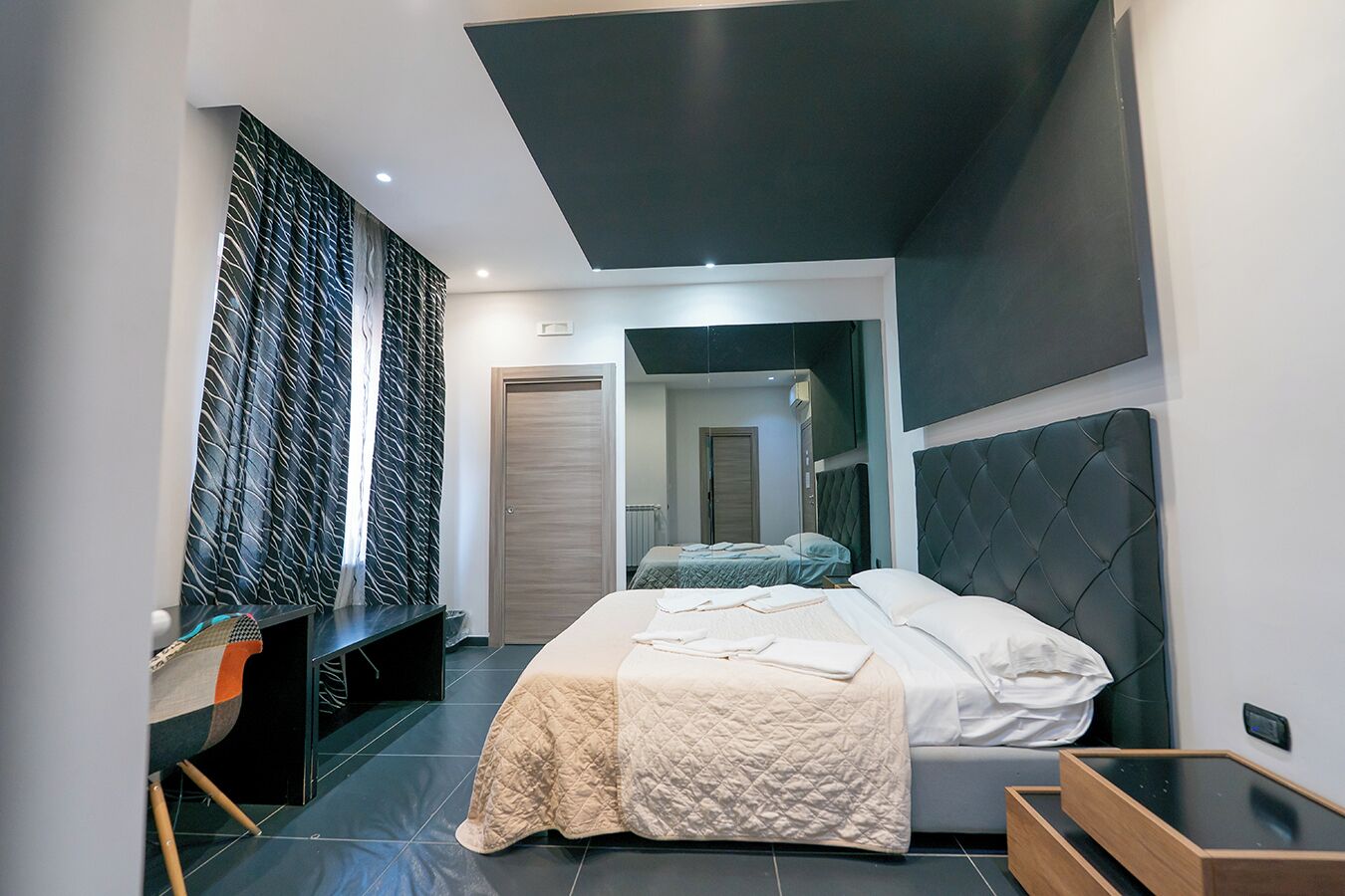 Quarto moderno com cama, mesas de cabeceira, escrivaninha e espelho.