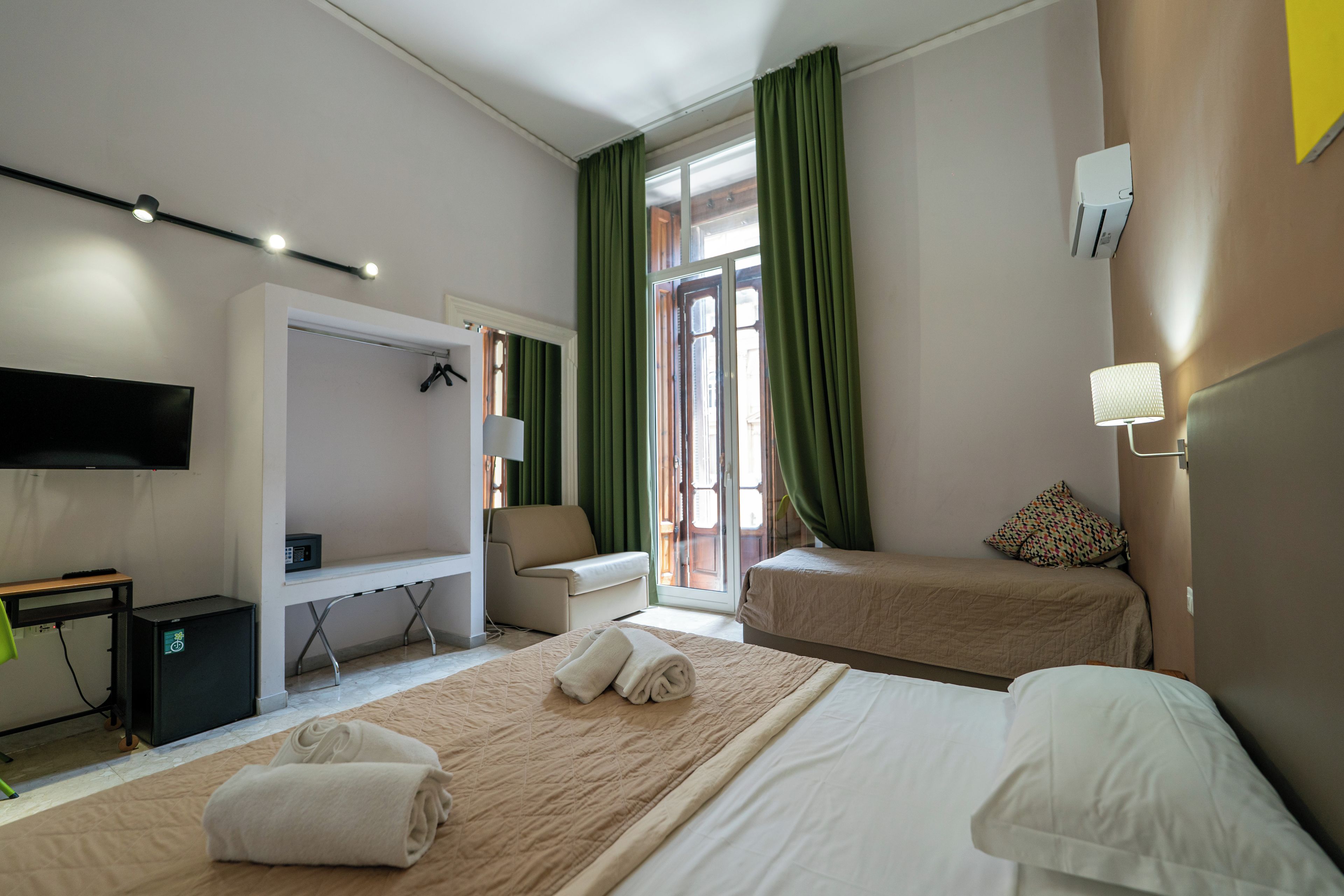 Quarto de hotel com cama, escrivaninha, televisão e janela com cortinas.