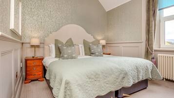 Quarto com cama, mesas de cabeceira, penteadeira e janela com cortinas.