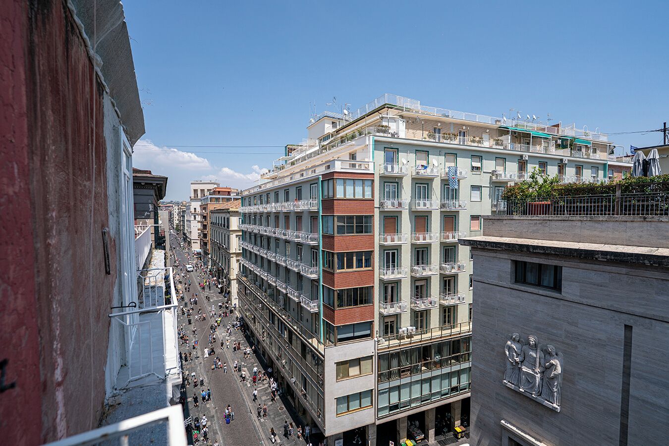Um edifício com várias andares e varandas, uma rua em frente e céu claro.