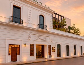 Um edifício de dois andares com estilo arquitetônico clássico, destacando uma entrada imponente com porta de madeira e uma varanda com grades pretas.
