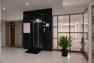 Um saguão de hotel com um elevador preto, um sinal de diretório do prédio e um vaso de plantas.